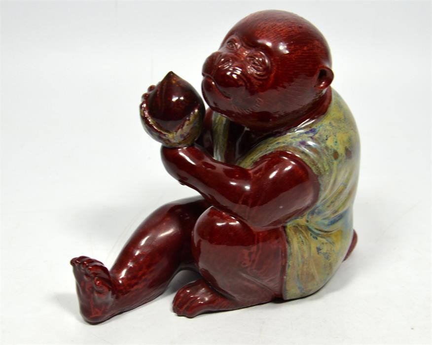 A Bernard Moore seated monkey in a flambe glaze, holding an artichoke ...