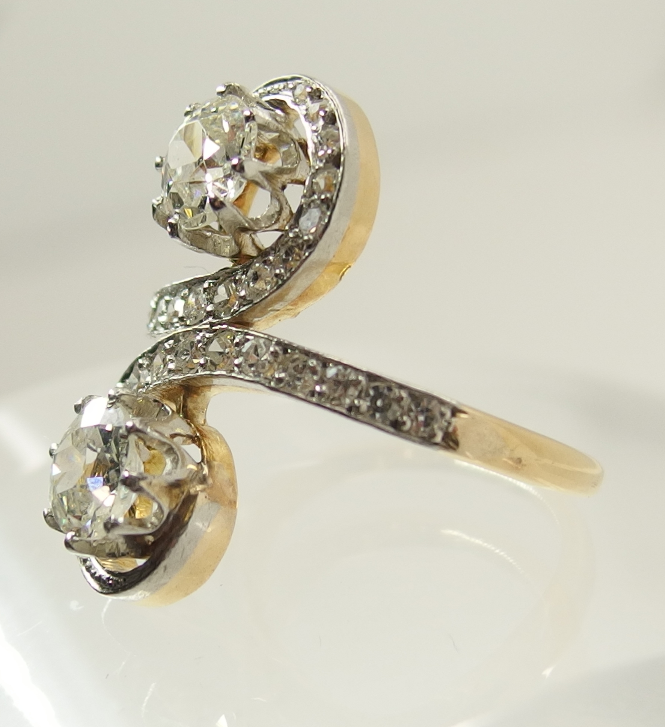 A TWIN DIAMOND SCROLL SHAPED RING set in yellow and white metal, the ...
