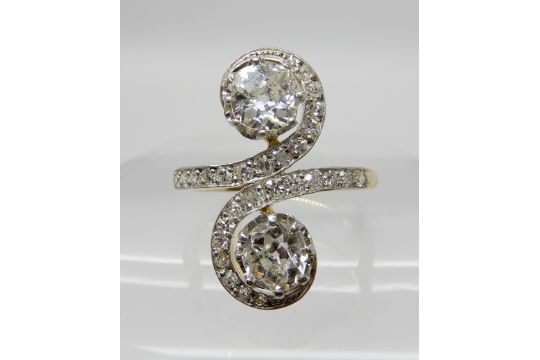 A TWIN DIAMOND SCROLL SHAPED RING set in yellow and white metal, the ...