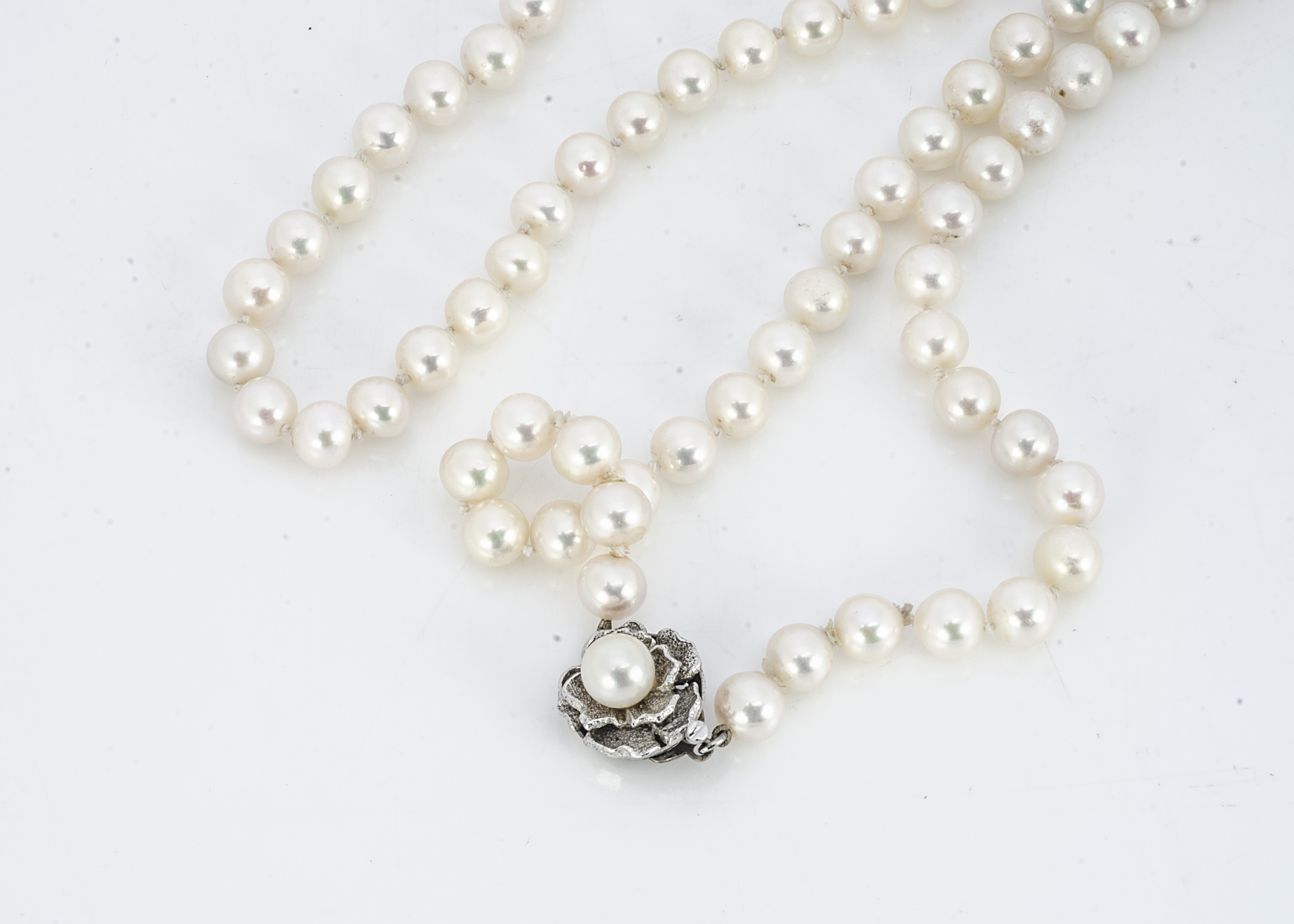 A string of uniform knotted strung cultured pearls, on a silver floral ...