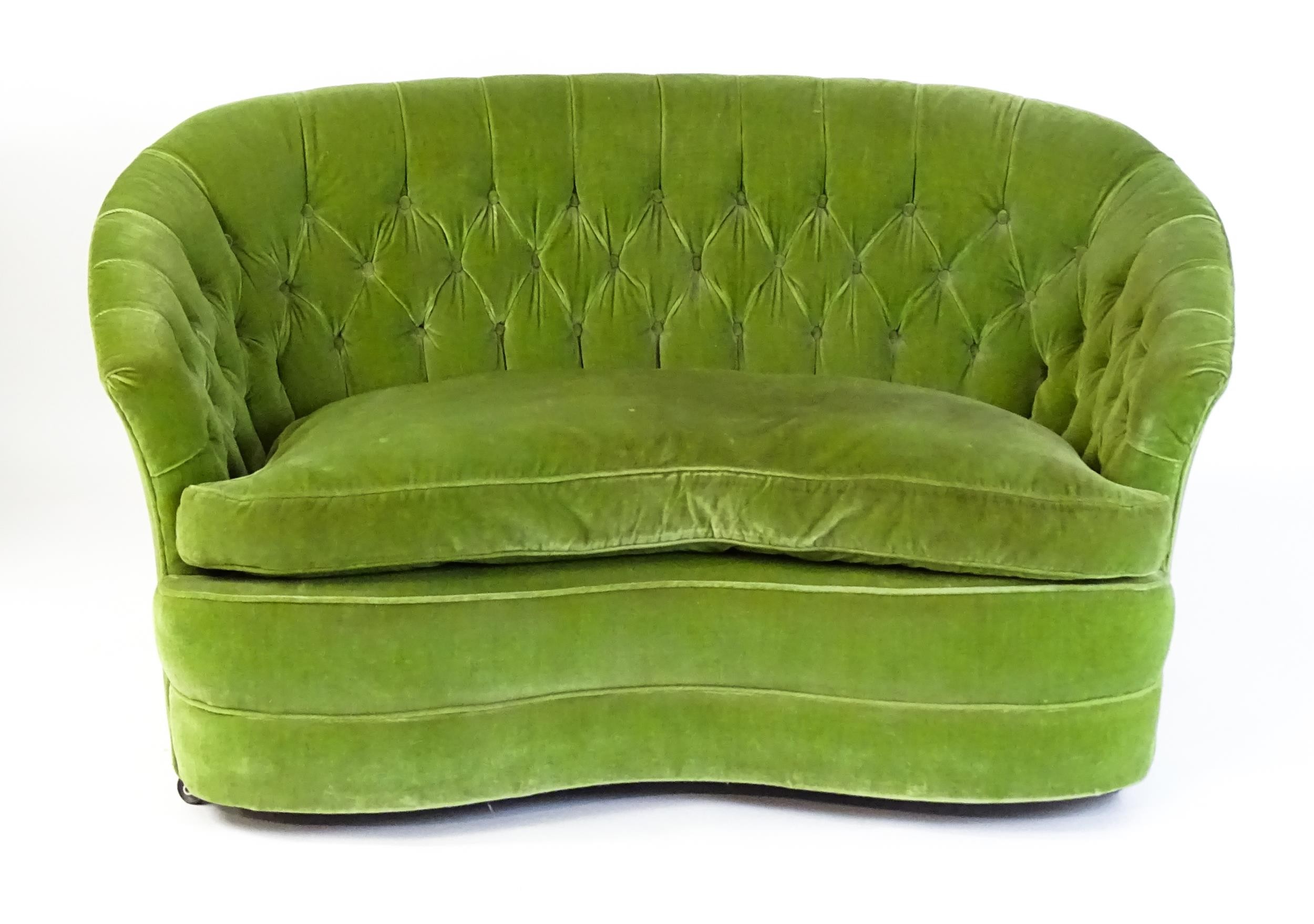 A 20thC kidney shaped sofa with deep buttoned upholstery and raised on ...