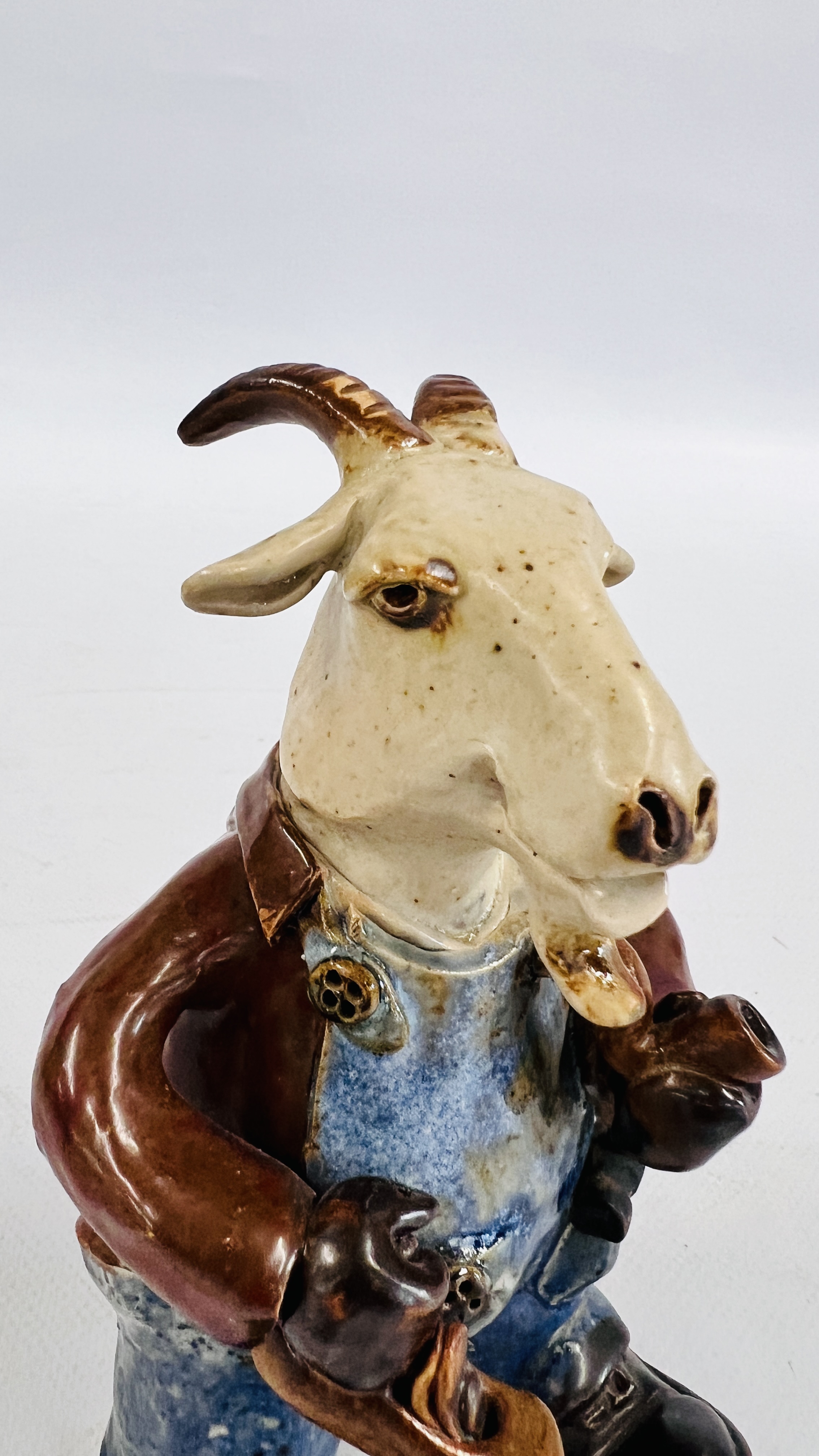 A MODERN STUDIO POTTERY FIGURE OF A CARPENTER GOAT WEARING BLUE ...