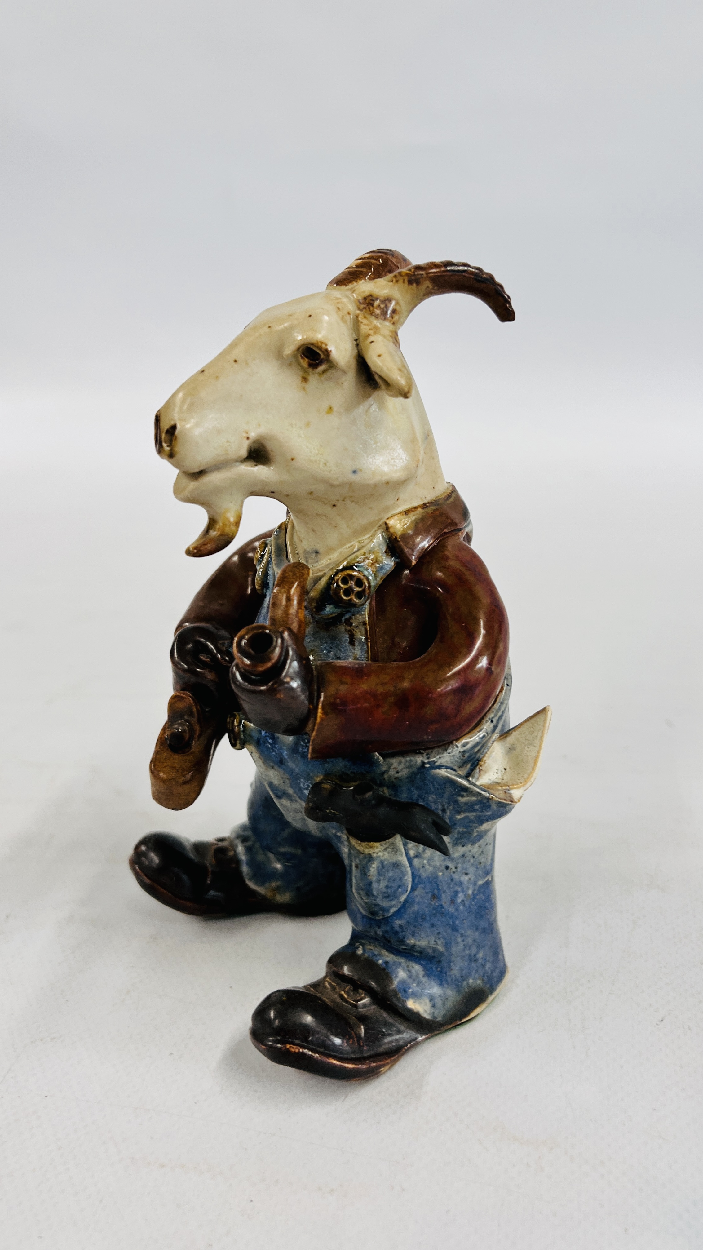 A MODERN STUDIO POTTERY FIGURE OF A CARPENTER GOAT WEARING BLUE ...