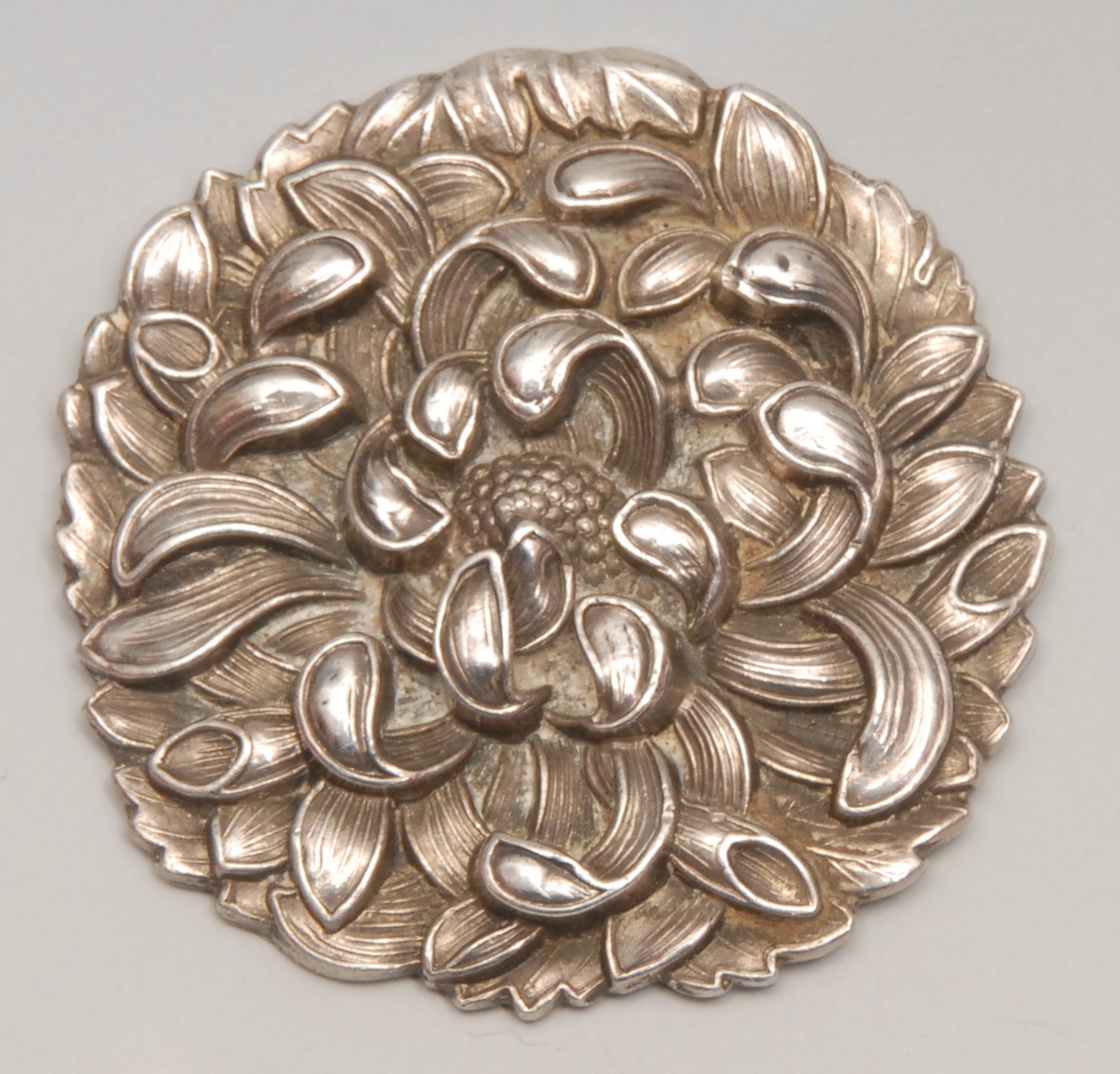 A Japanese silver buckle, as a chrysanthemum, 5cm diam, character mark ...