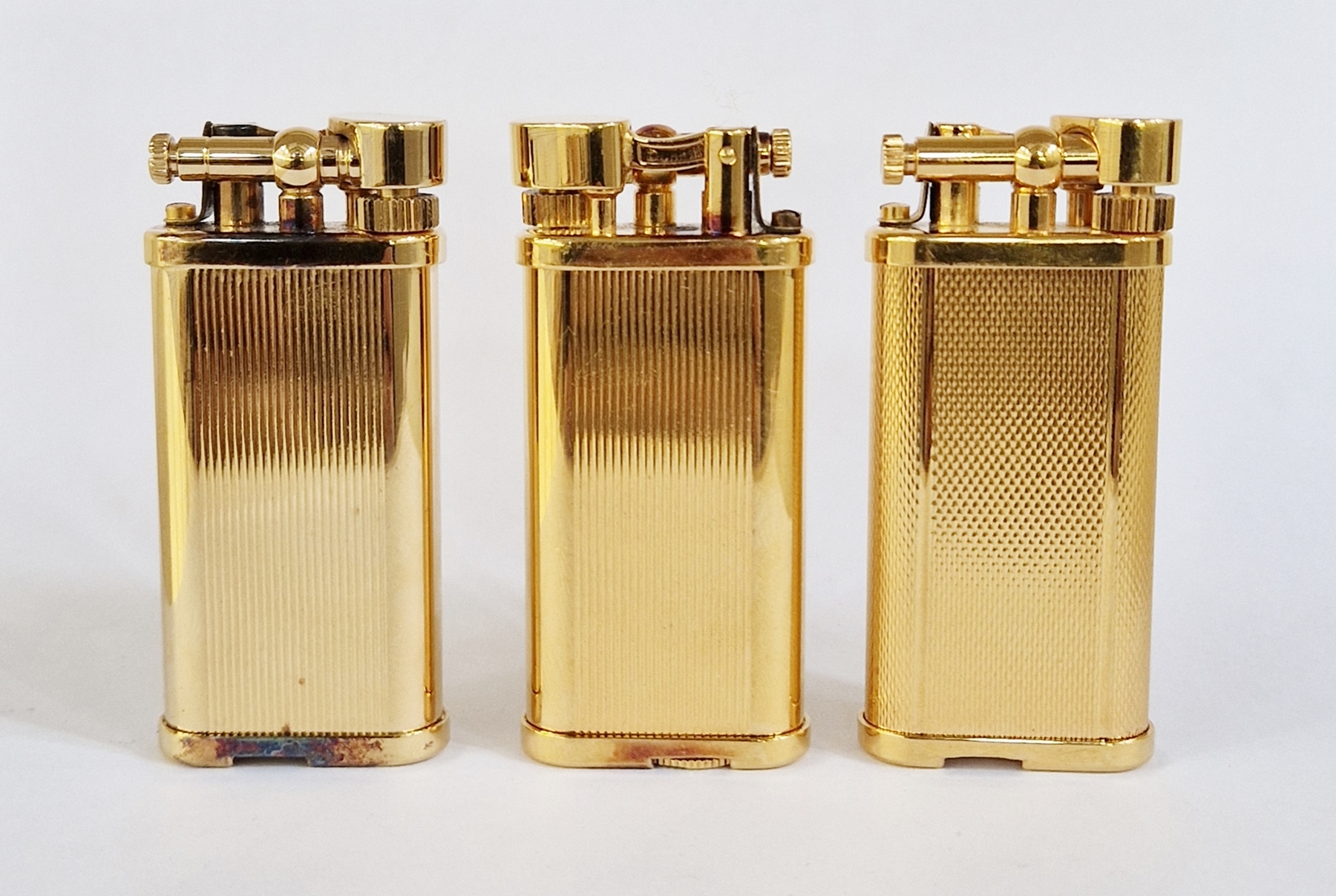Three Dunhill gilt metal lighters with engine-turned decoration, no ...