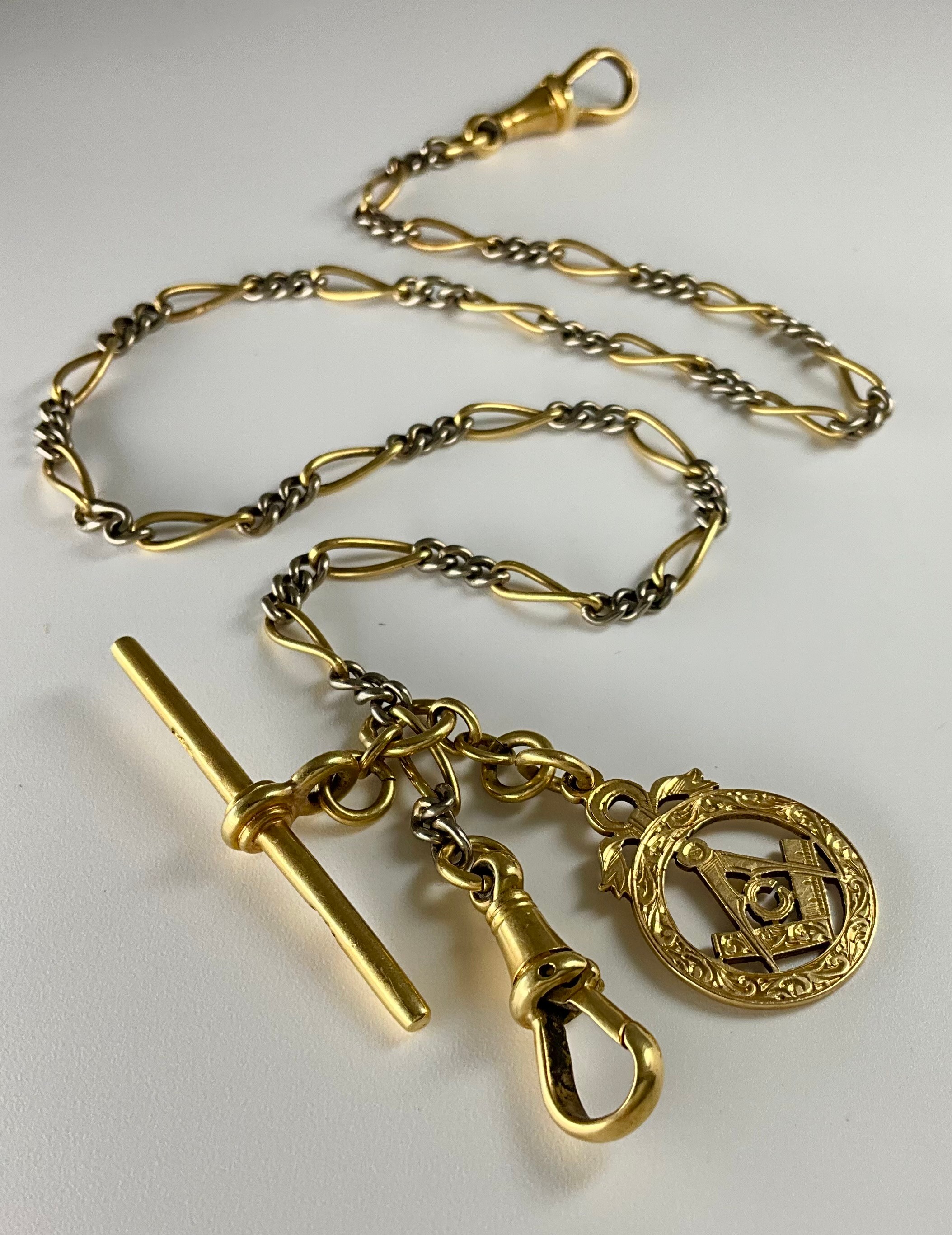 A tested 18ct yellow and white gold figaro chain with t-bar ...
