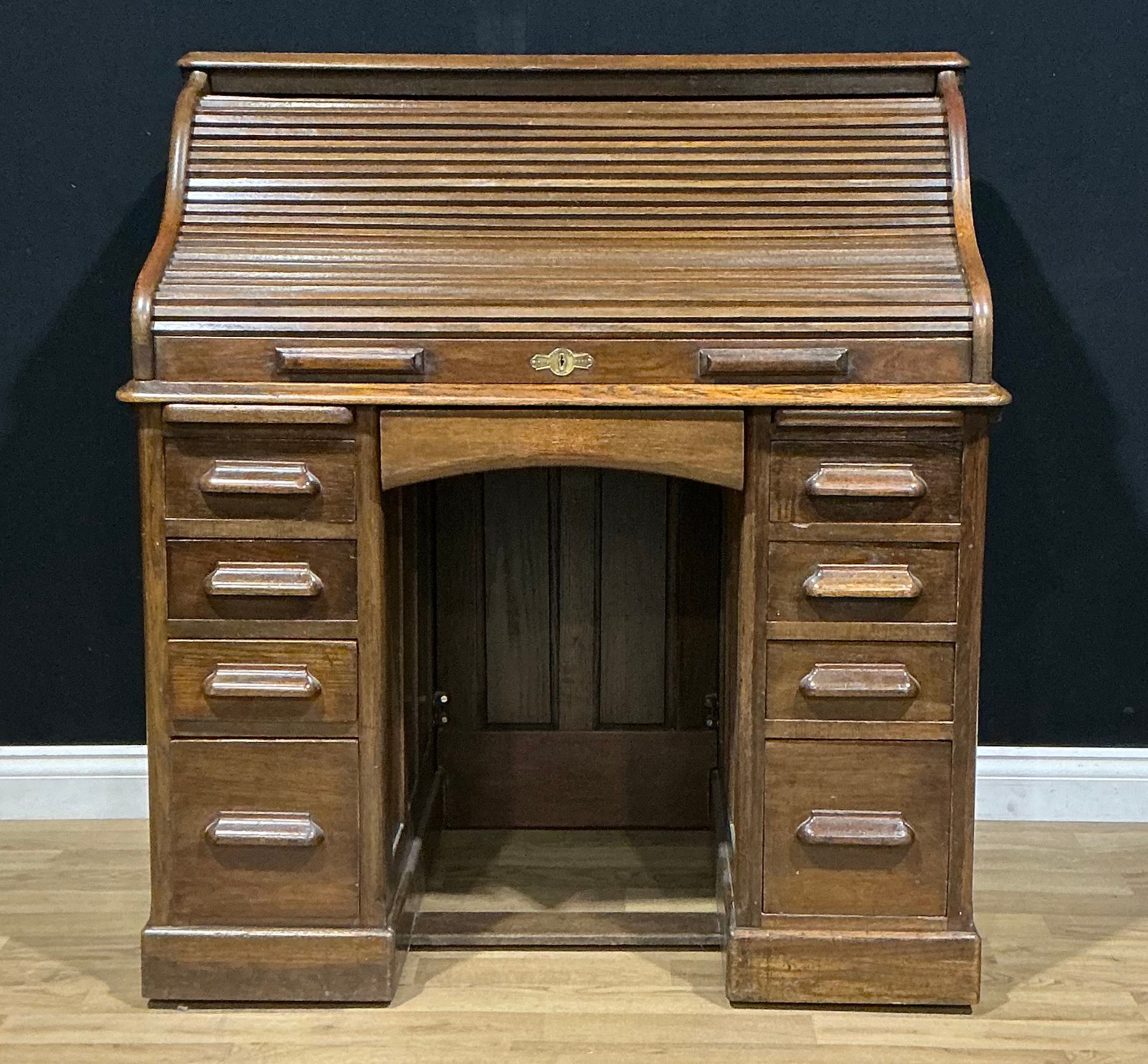 An early 20th century oak roll top desk, the shaped tambour enclosing a ...