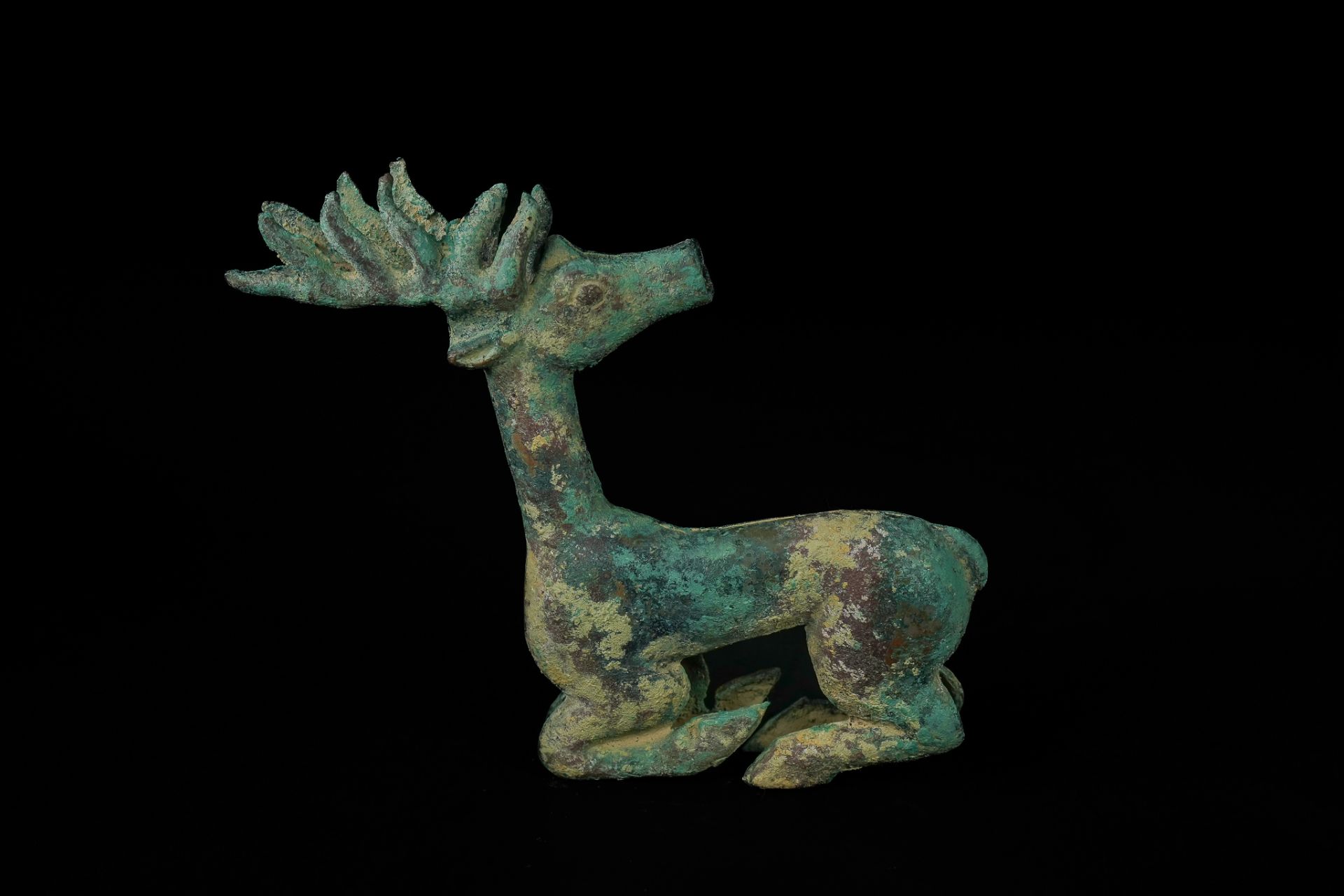 A bronze figurine depicting a kneeling or couchant deer or stag ...