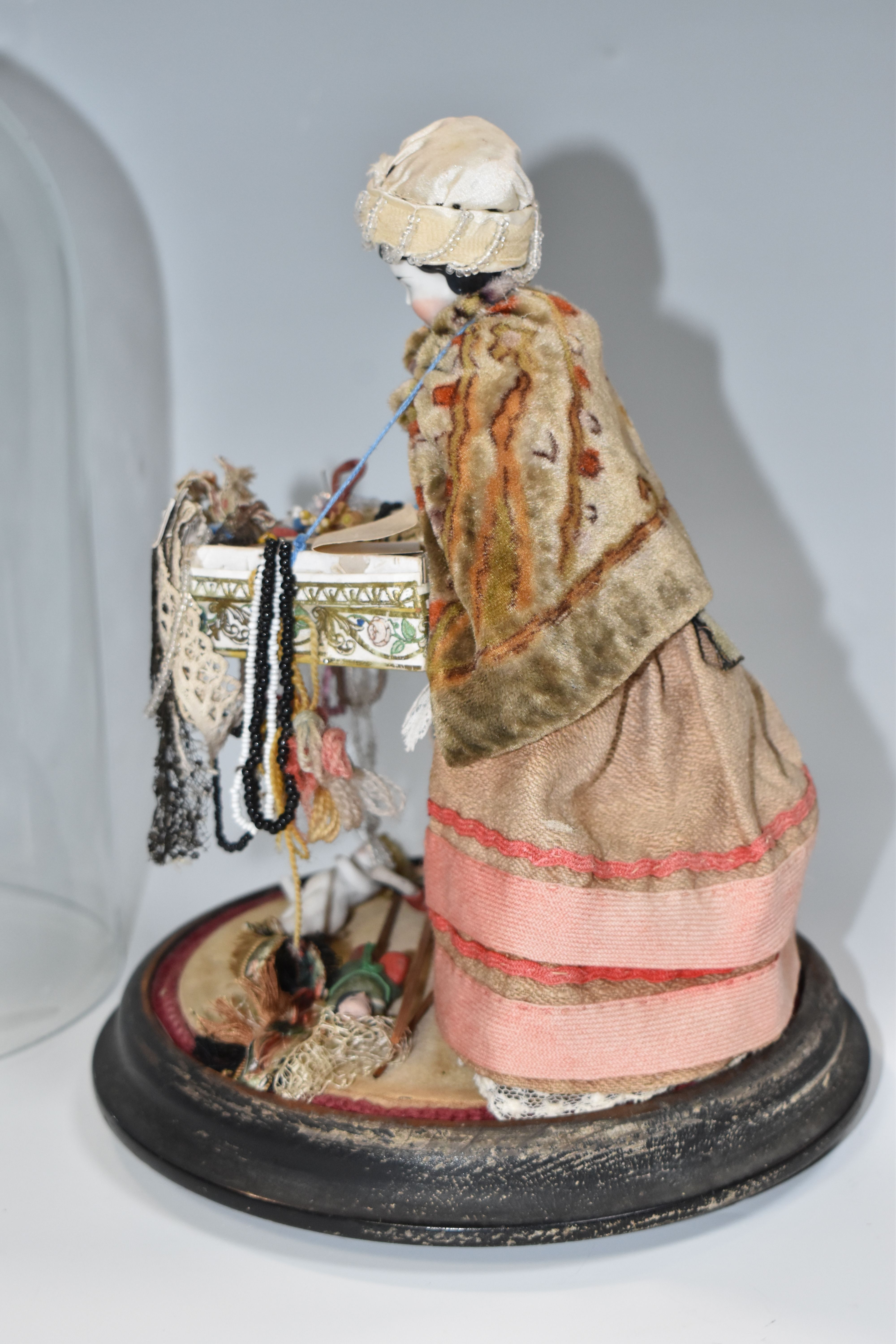 A GLASS DOMED NINETEENTH CENTURY PEDLAR DOLL on a wooden base with a ...