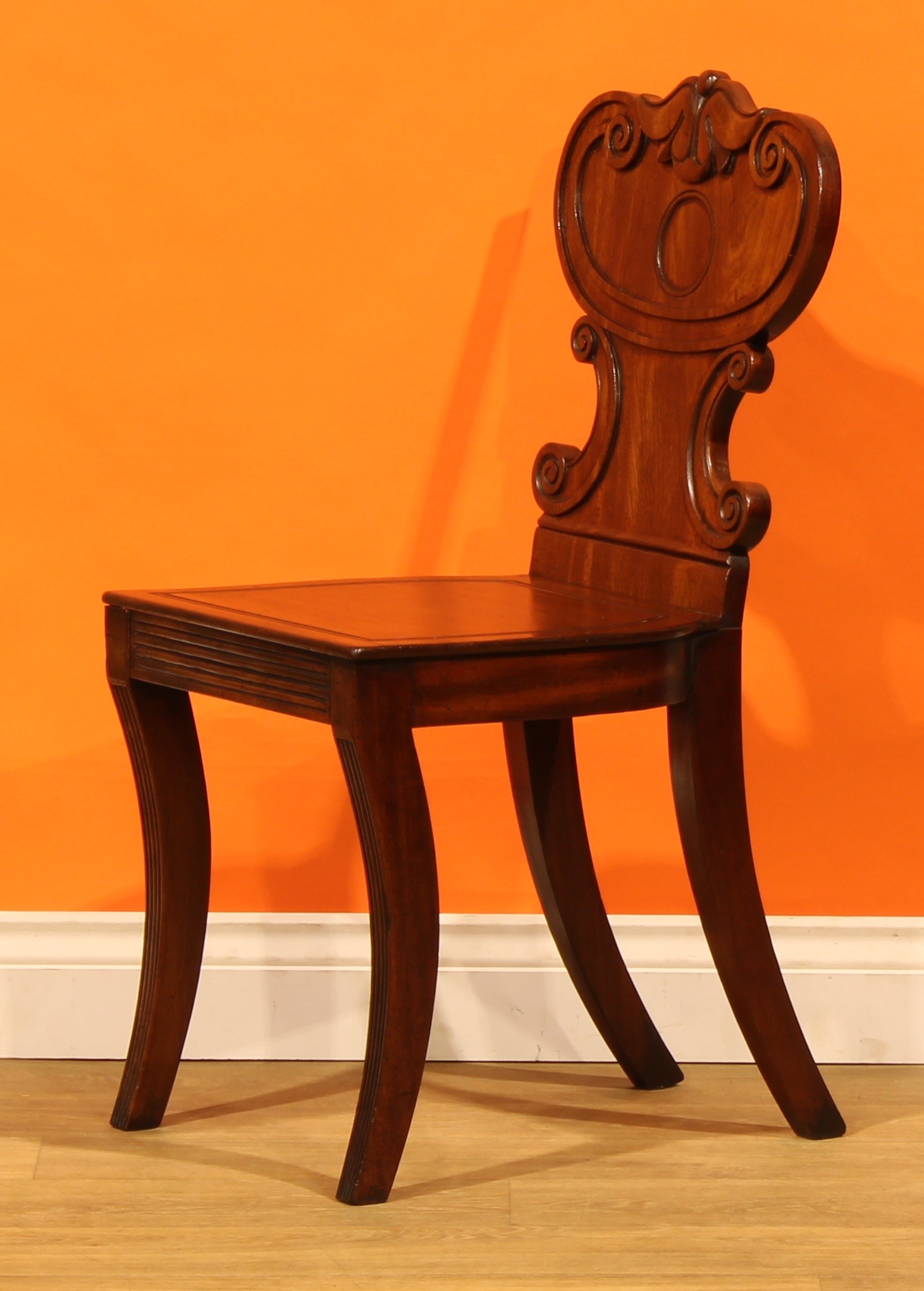 A pair of George/William IV mahogany hall chairs, each back carved with ...