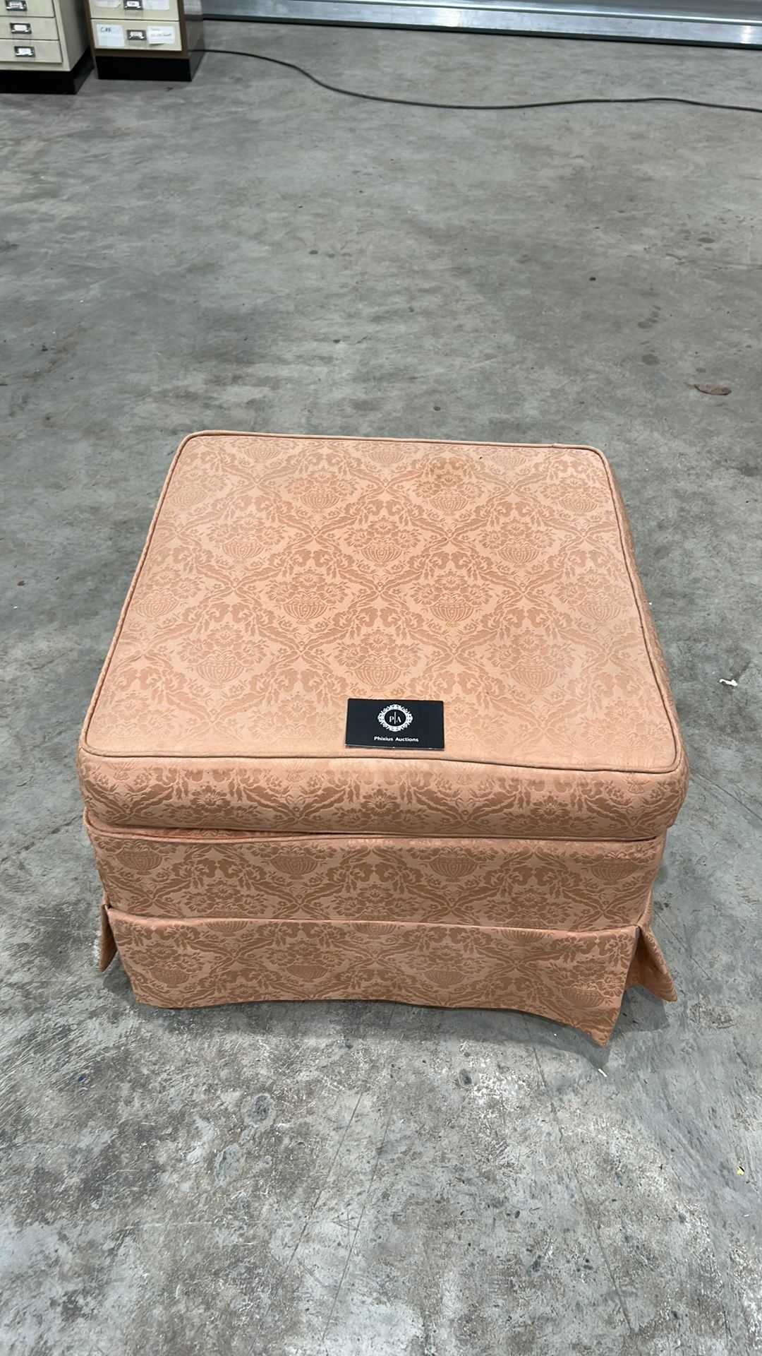 A square upholstered ottoman or footstool, in peach damask textile with ...